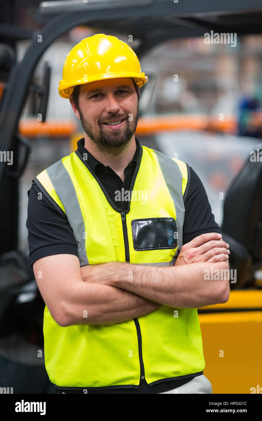 Portrait of smiling factory worker standing with arms crossed in ...