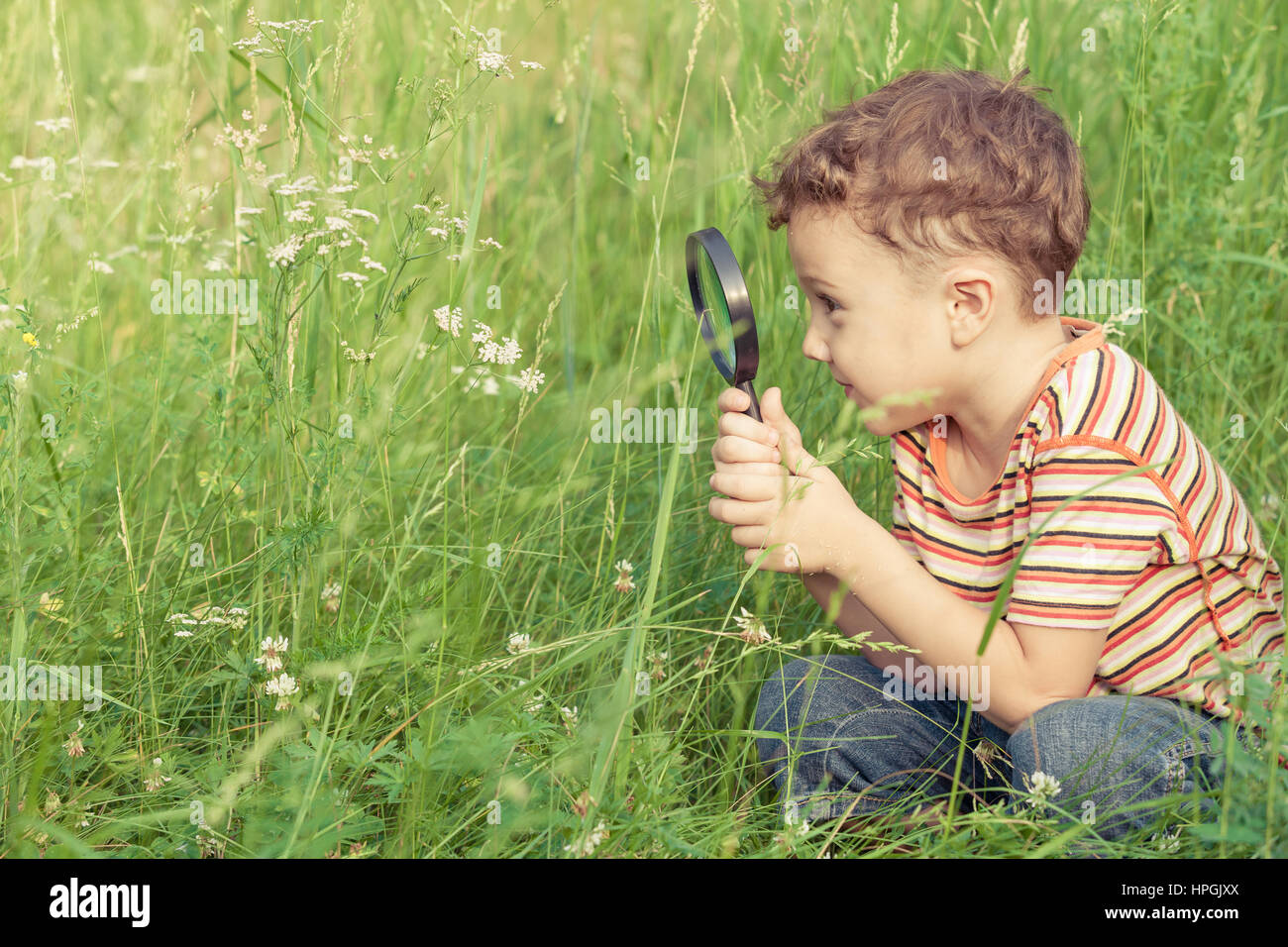 Happy little boy exploring nature with magnifying glass at the day time ...