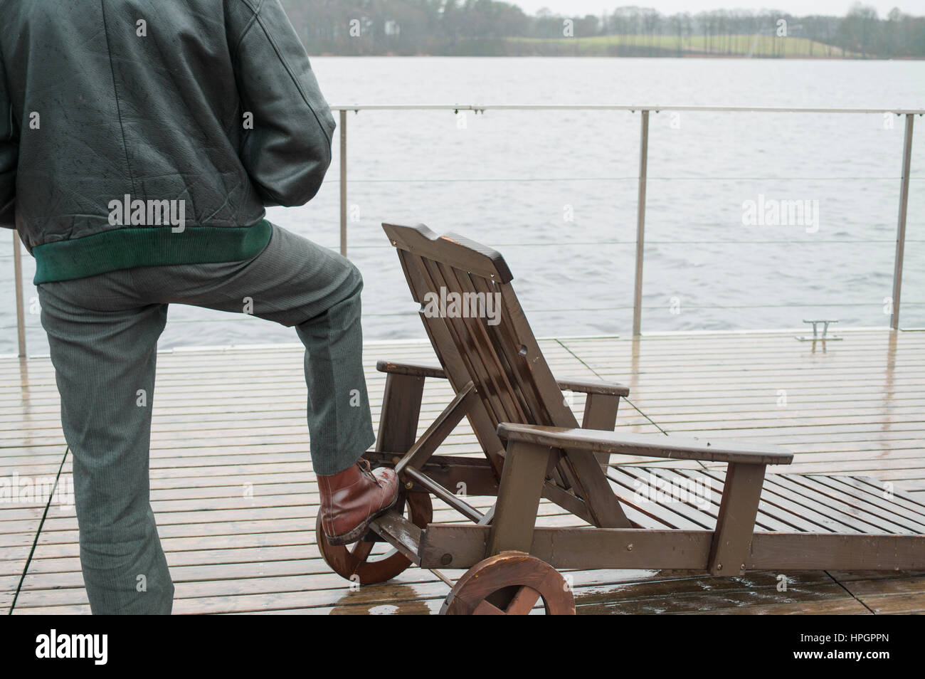Man standing on the wet deck next to a beach lounger, outdoor rear ...