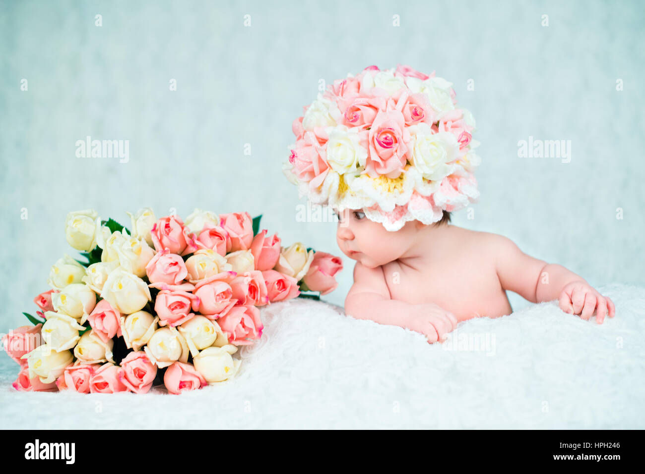 A newborn baby girl in the hat of the rose smiles. Portrait on a white ...