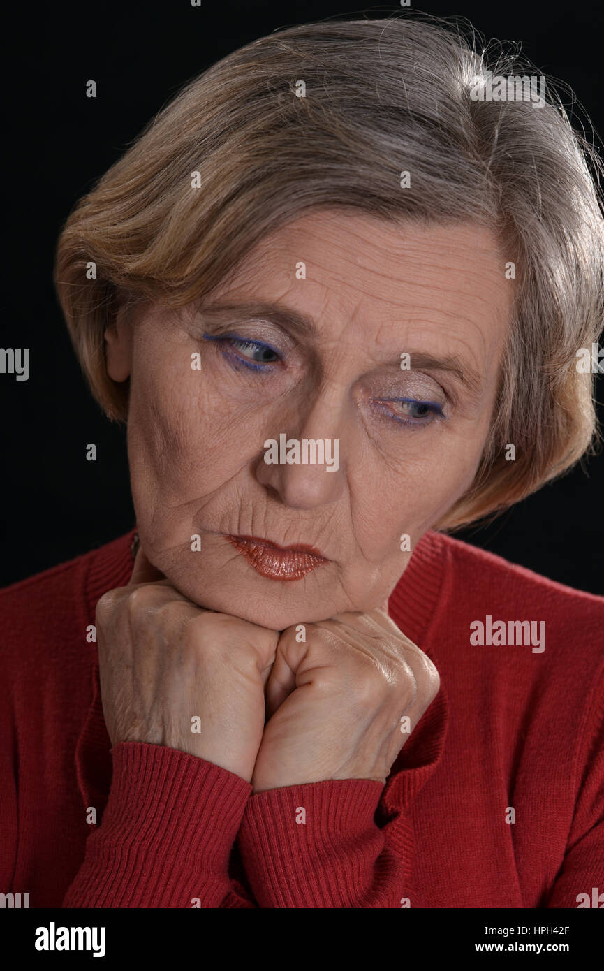 sad old woman in red on a black background Stock Photo - Alamy