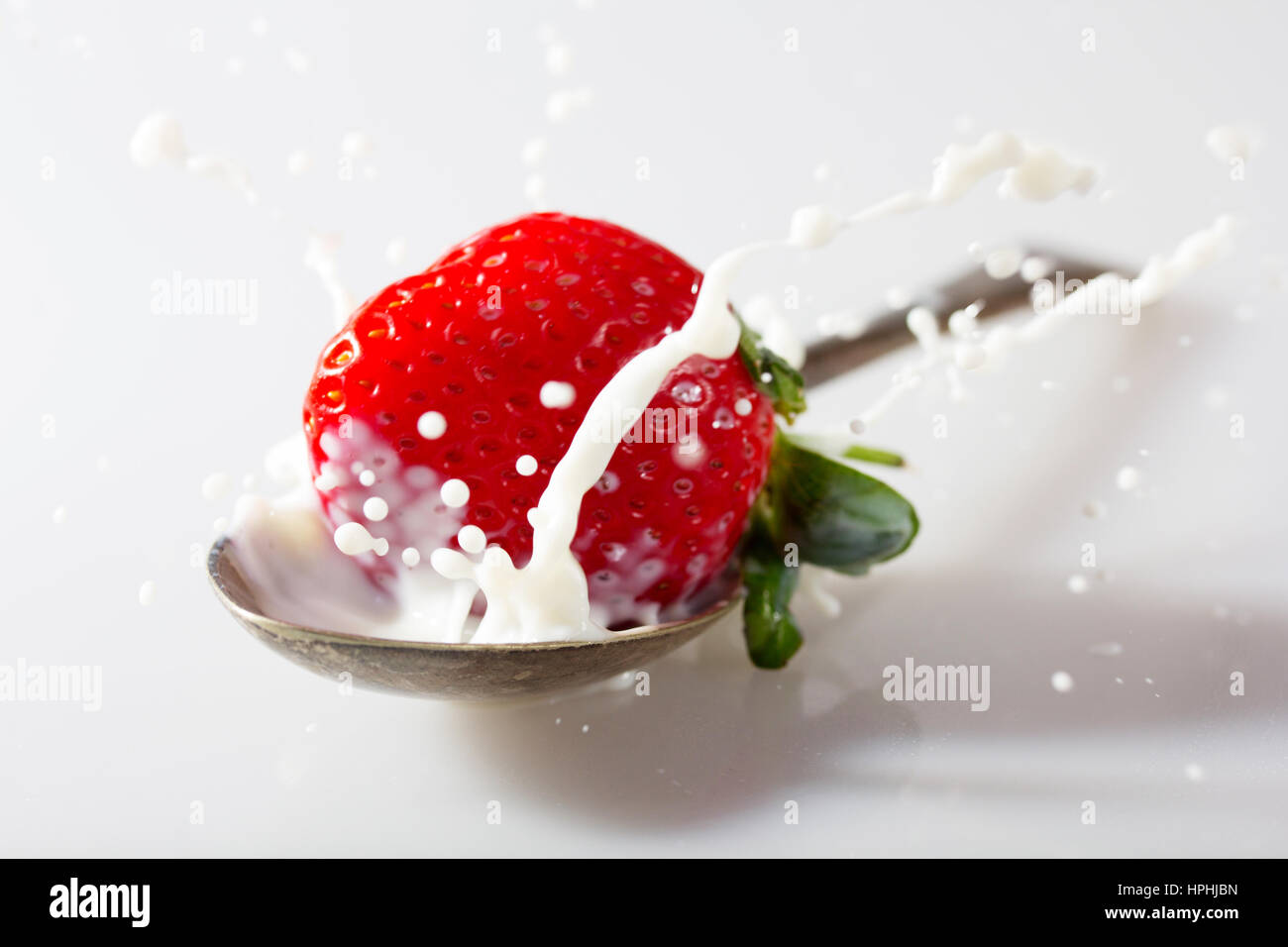 Strawberry falling into a spoon full of cream Stock Photo - Alamy
