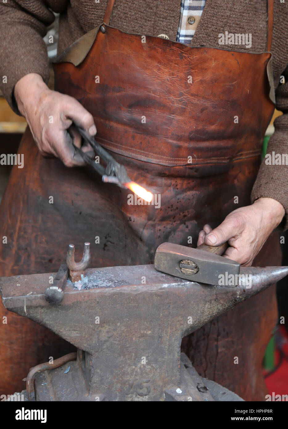 hands of an elderly blacksmith working iron with a hammer and the anvil ...