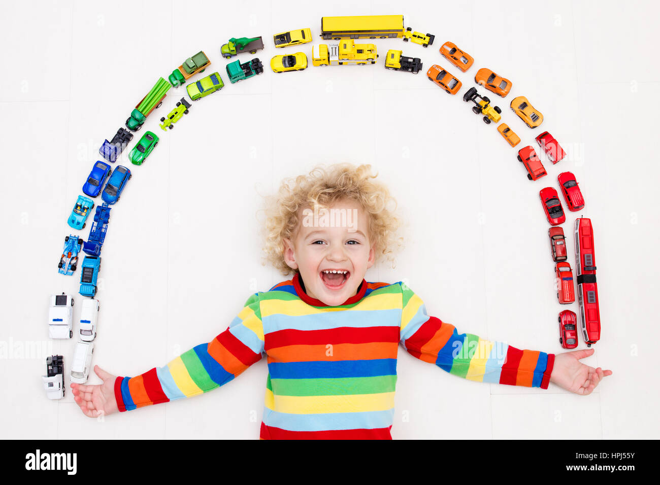 Funny curly toddler boy playing with his model car collection on the ...