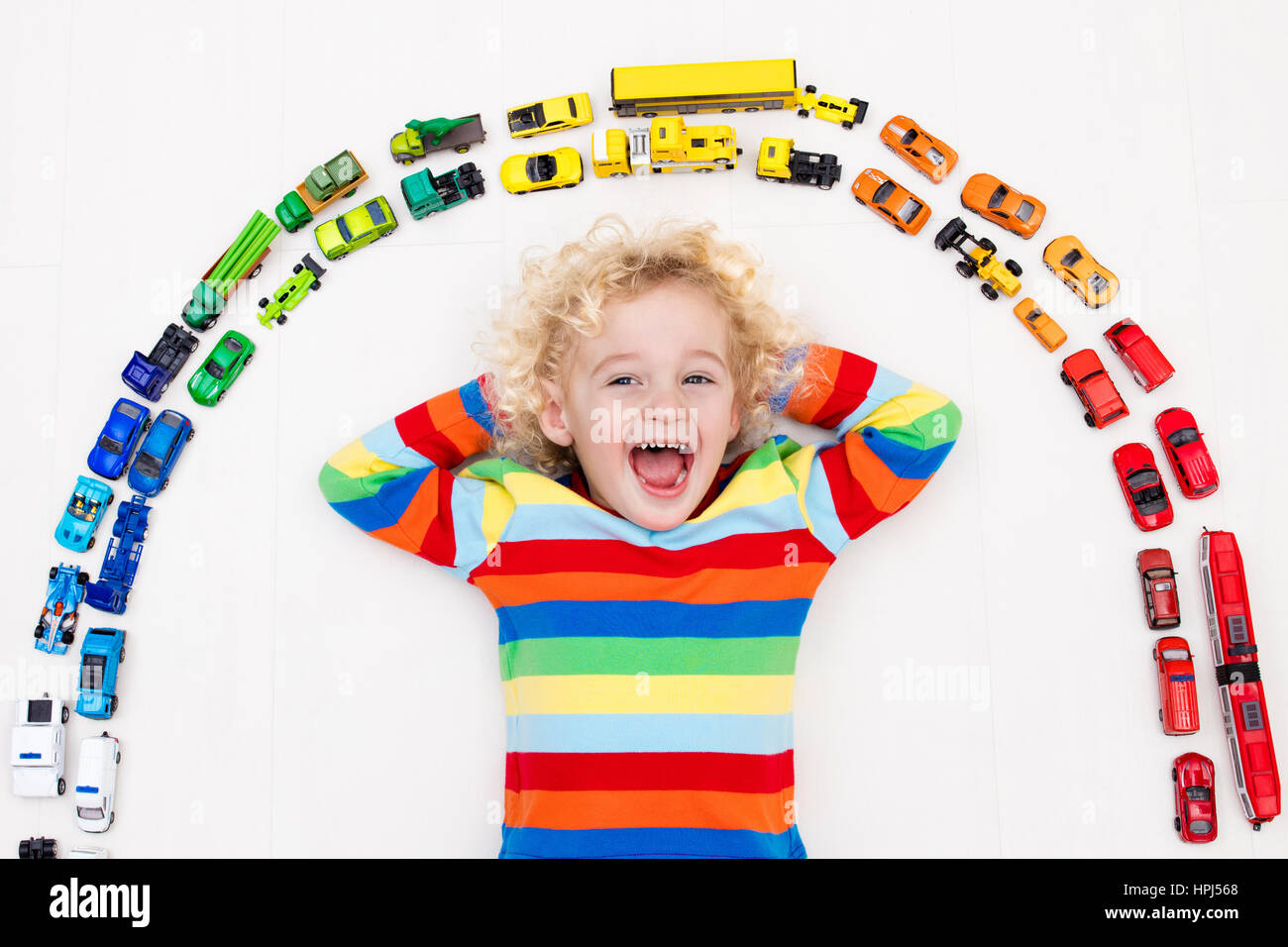Funny curly toddler boy playing with his model car collection on the ...