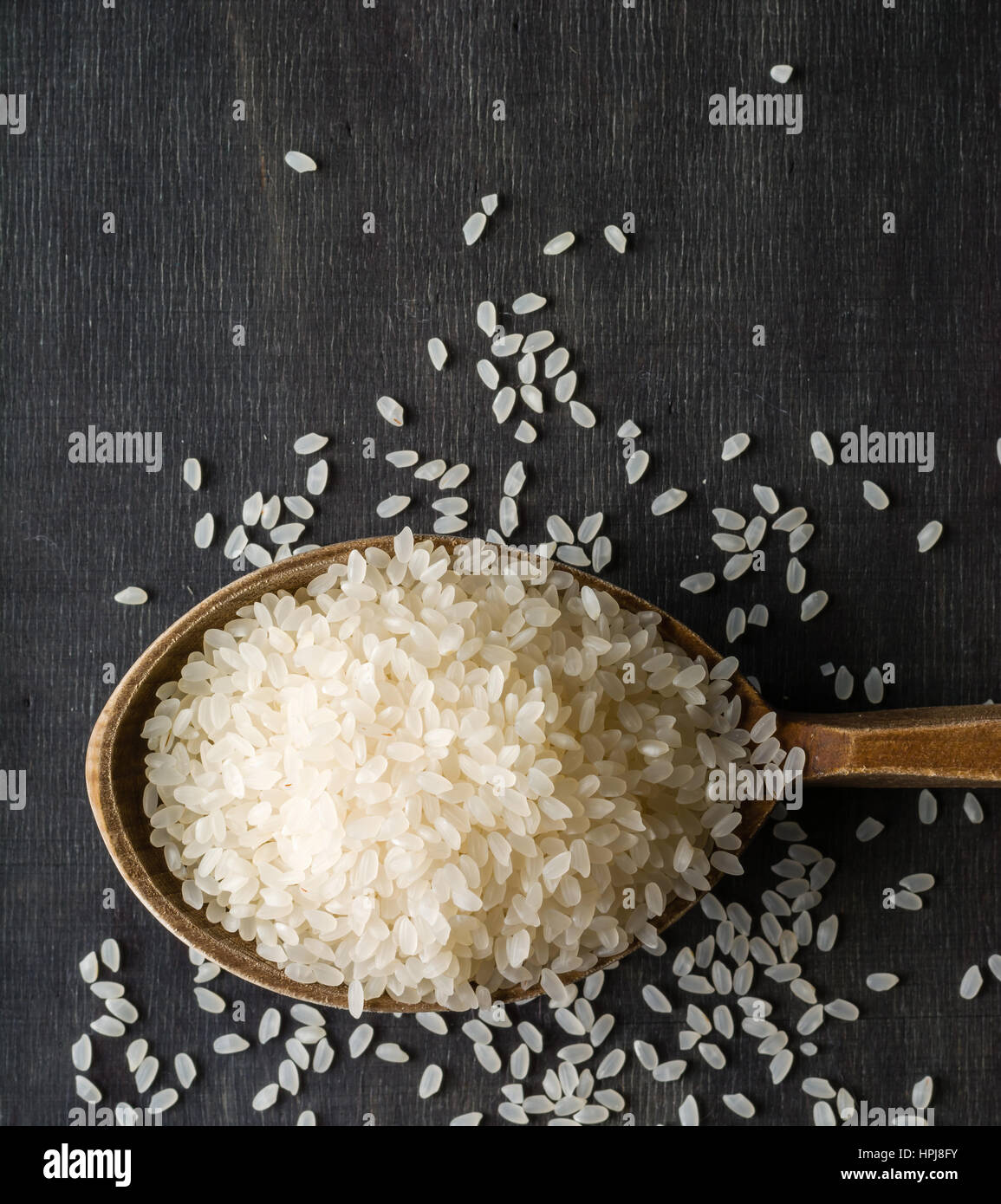 A handful of white polished rice in a wooden old spoon. Dark wood ...
