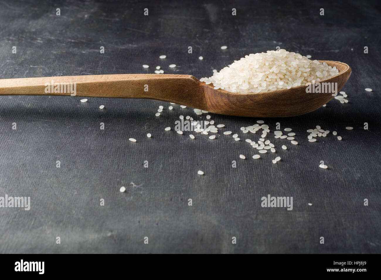 A handful of white polished rice in a wooden old spoon. Dark wood ...