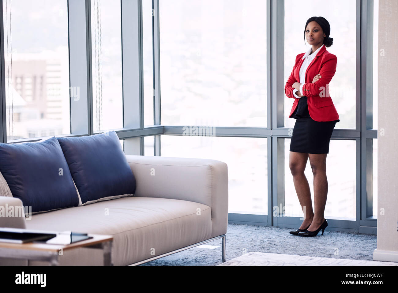 Wide full body shot of business woman standing next to large windows in ...