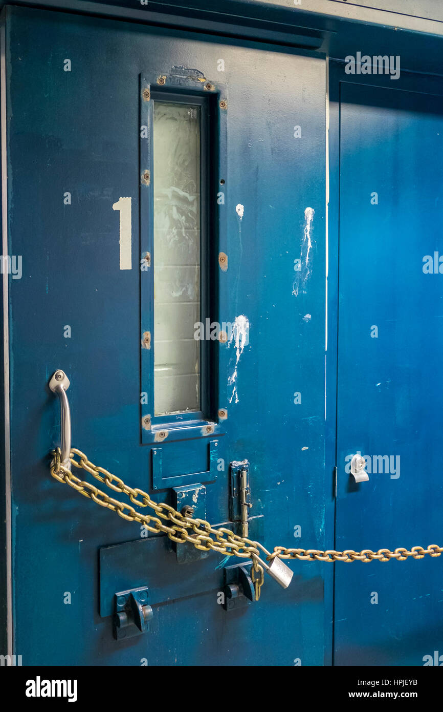 A heavy gold coloured chain is padlocked to a handle of a blue prison ...