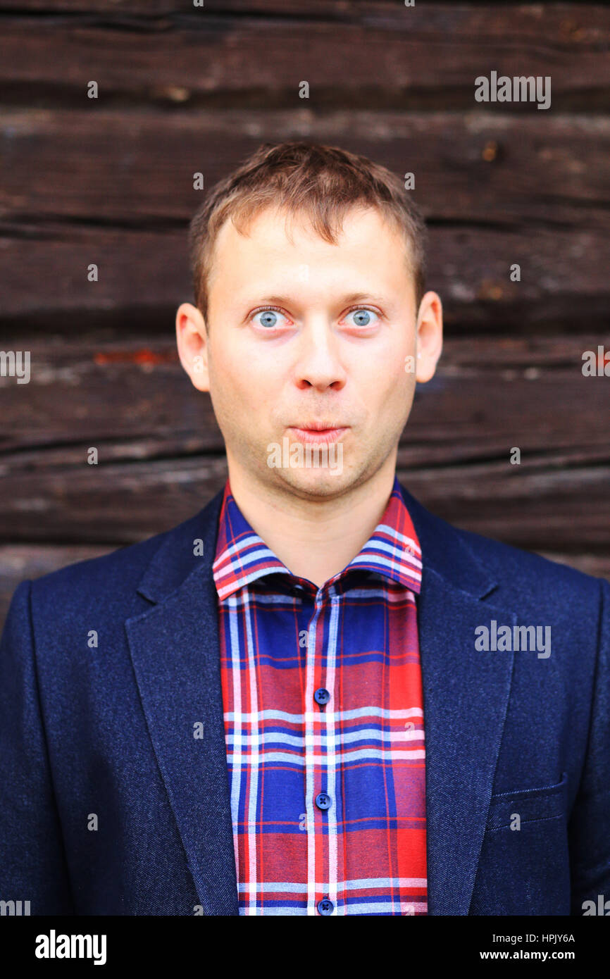 Surprised man in blue jacket and checkered shirt on wood background ...
