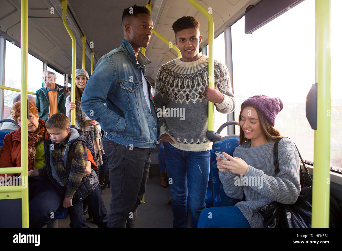 Two men are standing on a bus. There are people around them talking and ...