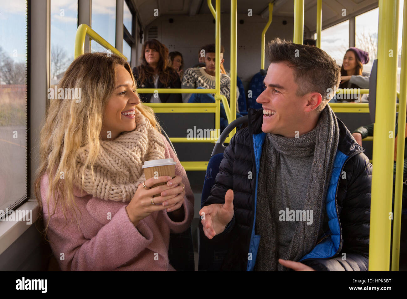 Young couple/friends chatting on a bus together. There are other people ...