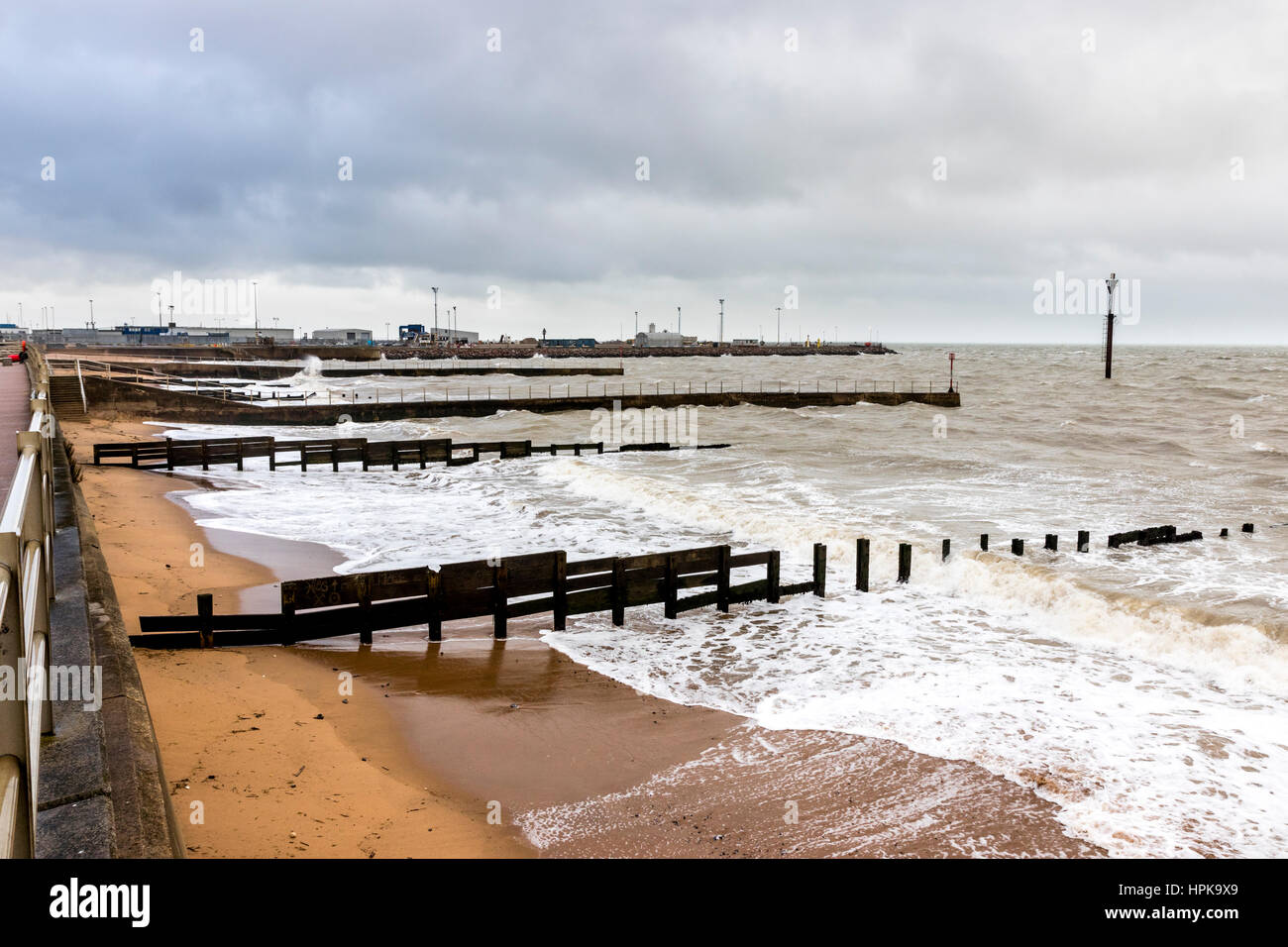 Sandy beach battered by rough seas during storm. Concrete and wooden ...
