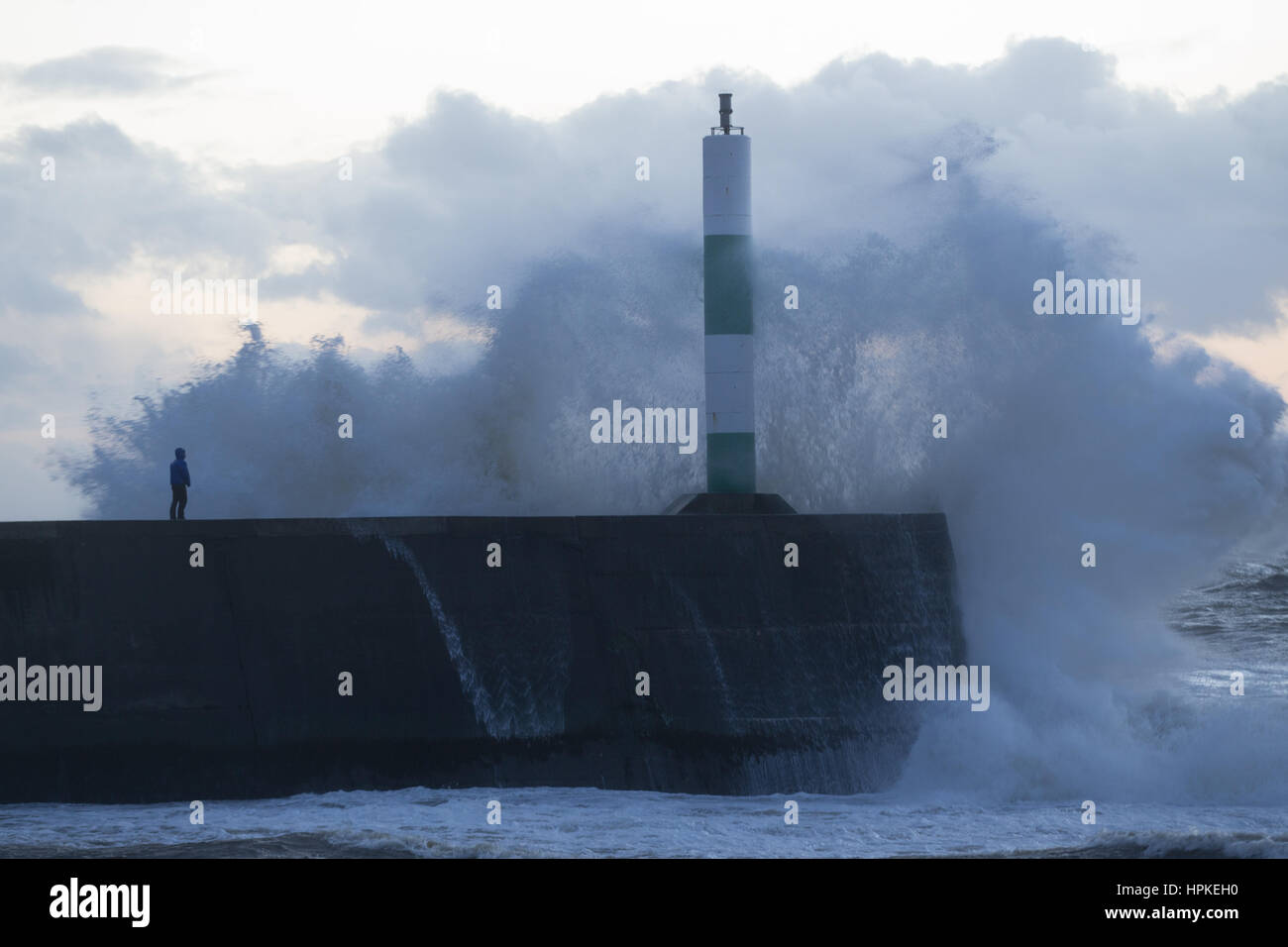 A man risking standing on a jetty as the big waves crash over him ...