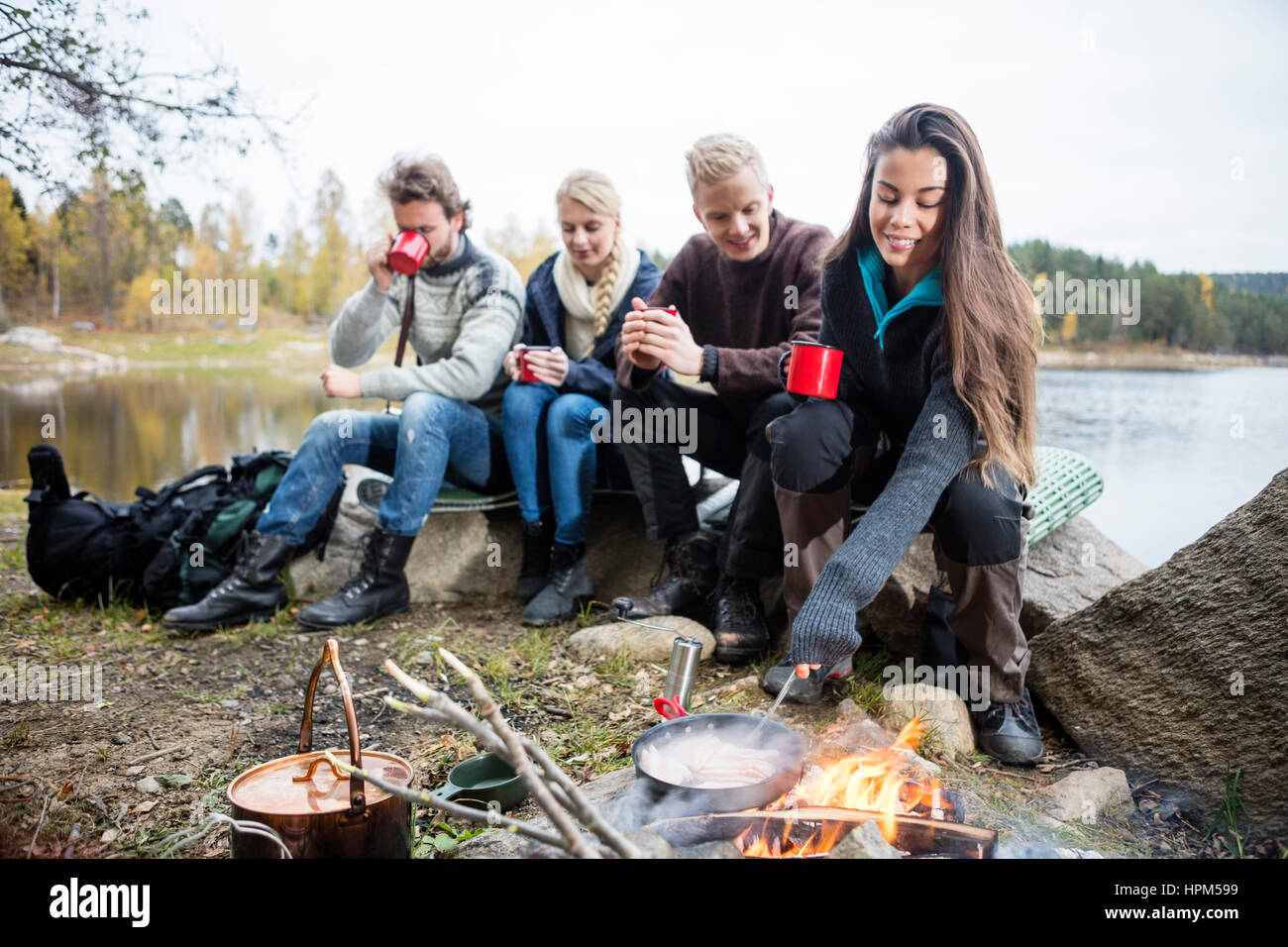 Young woman cooking food on campfire with friends in background at ...