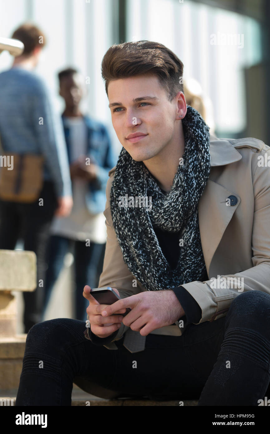 A happy young male smiles off camera as he relaxes in the city. He is ...