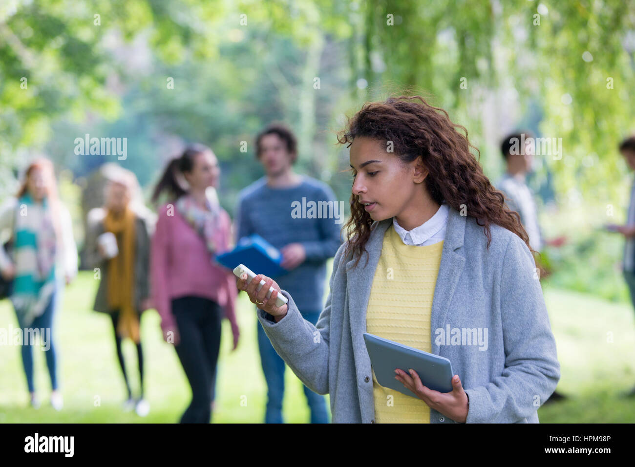 A happy young student smiles as she uses her mobile phone outdoors. She ...