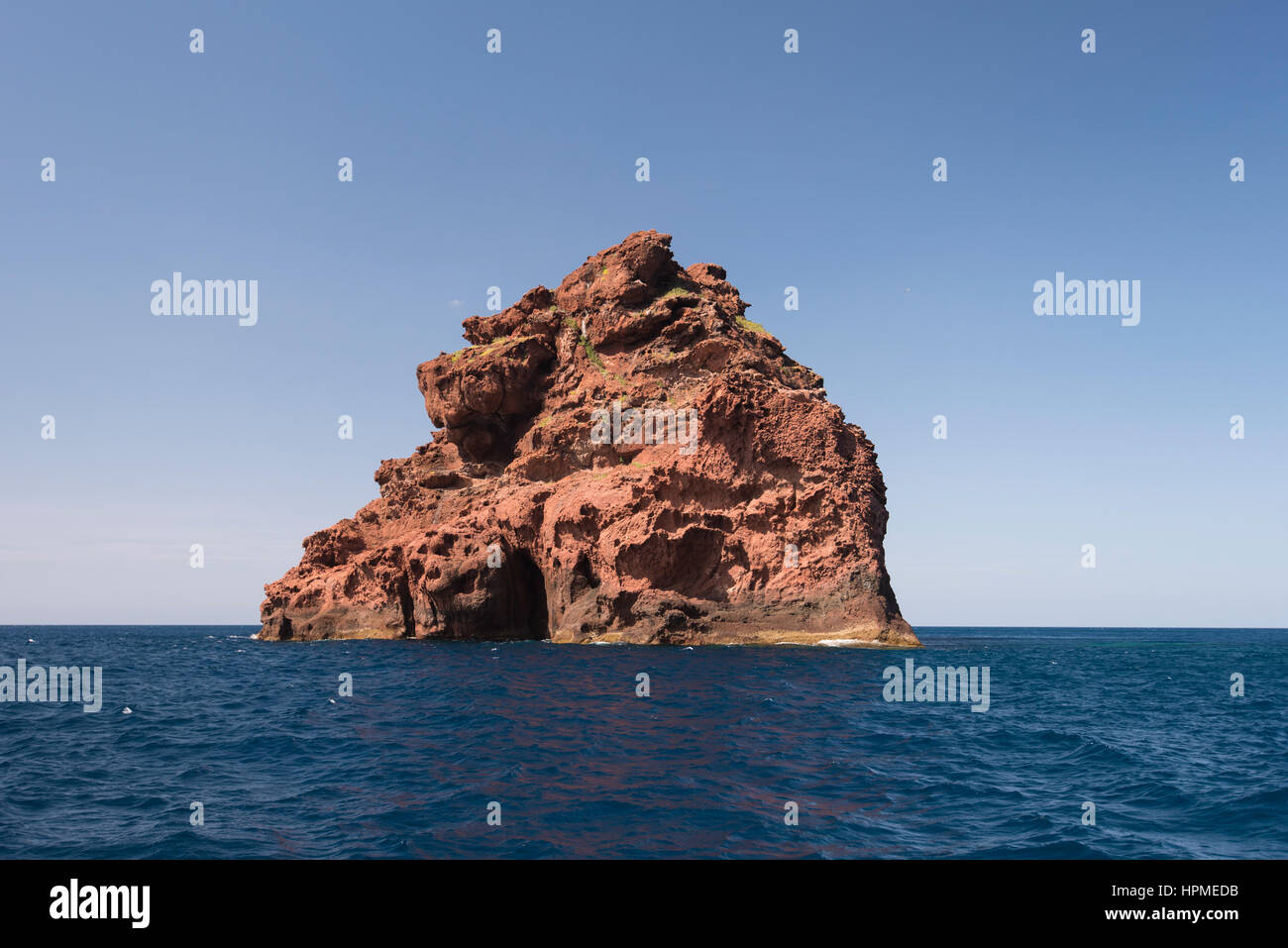 Volcanic red rock emerges from the transparent sea in the natural park ...
