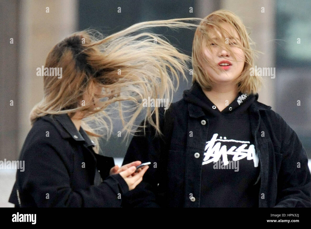 The hair of two young girls is caught in a gust of wind as they walk ...