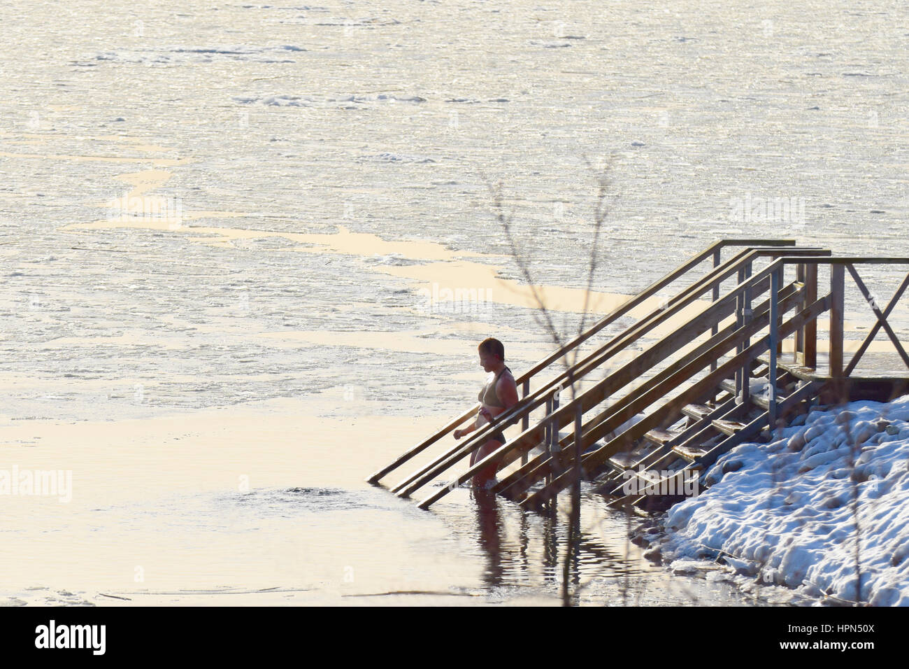 Winter swimming. Woman standing on stairs with her legs in cold water ...