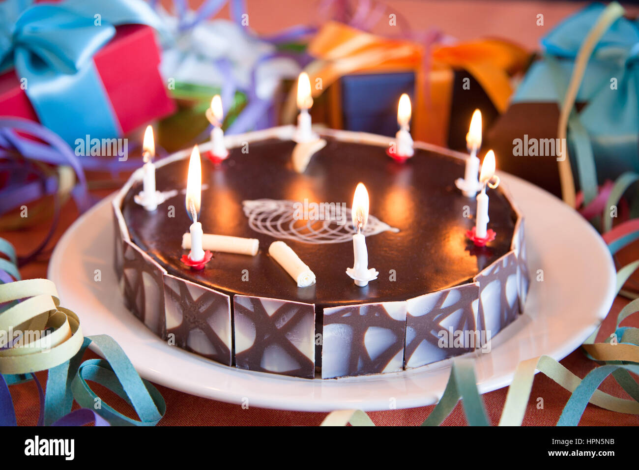 big chocolate cake with birthday candles burning between gift boxes ...