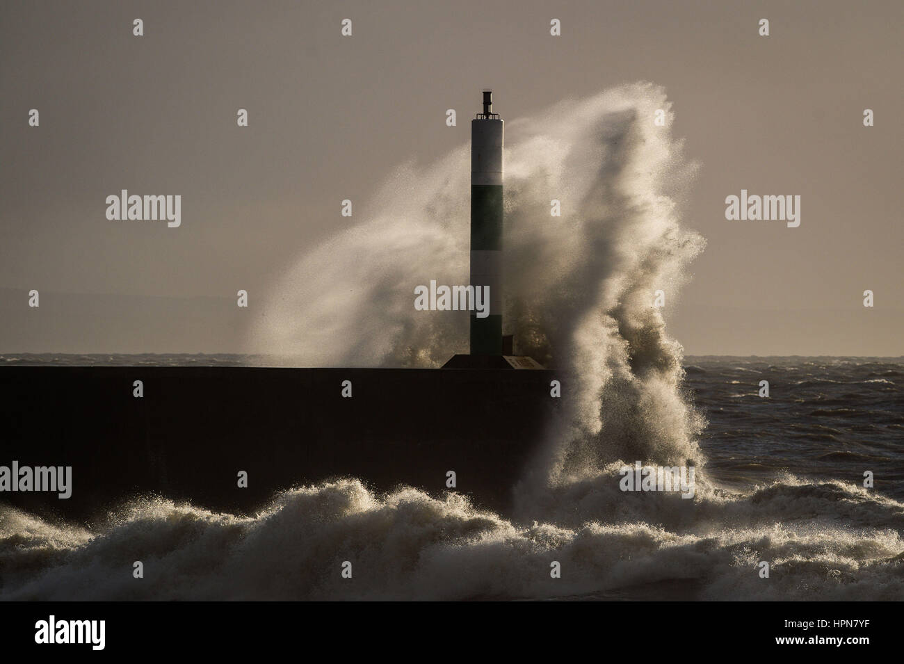 The lighthouse and harbour wall is battered by waves at Aberystwyth ...