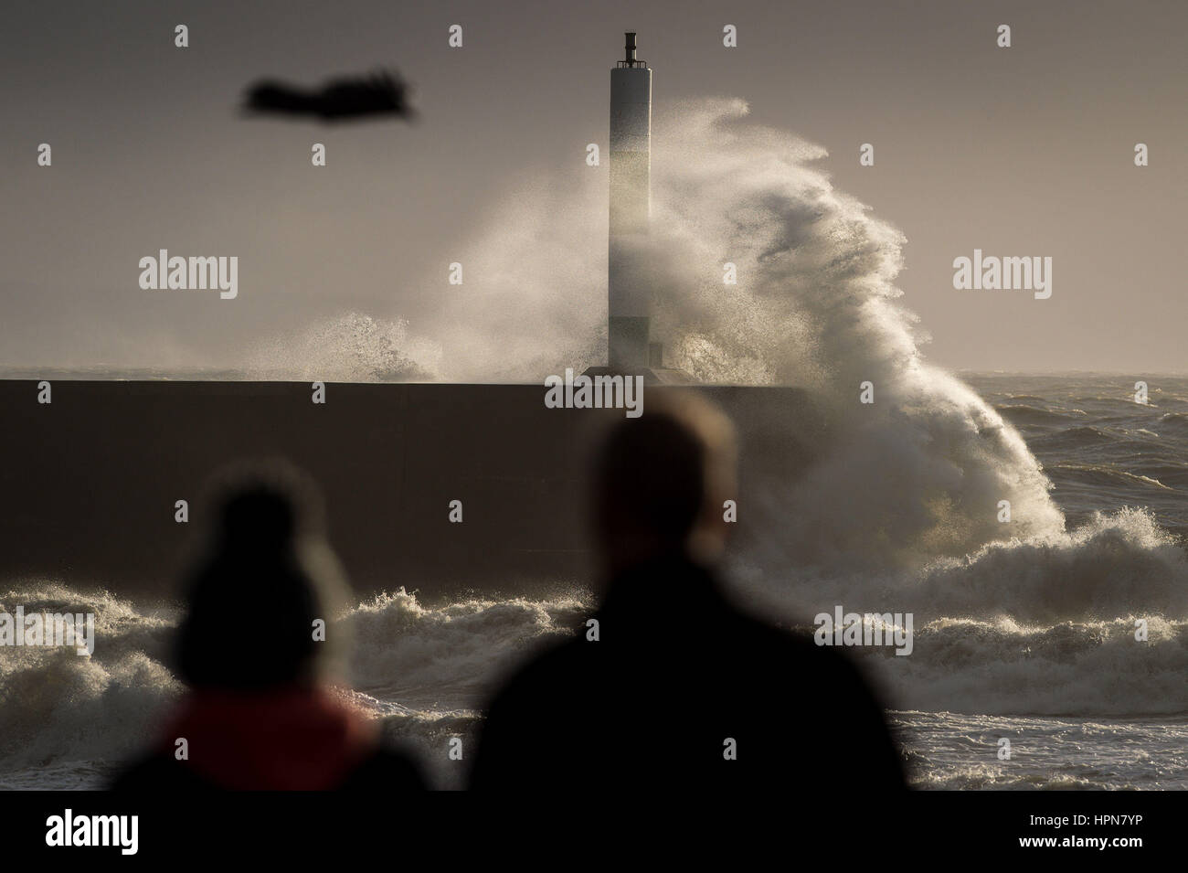 The lighthouse and harbour wall is battered by waves at Aberystwyth ...