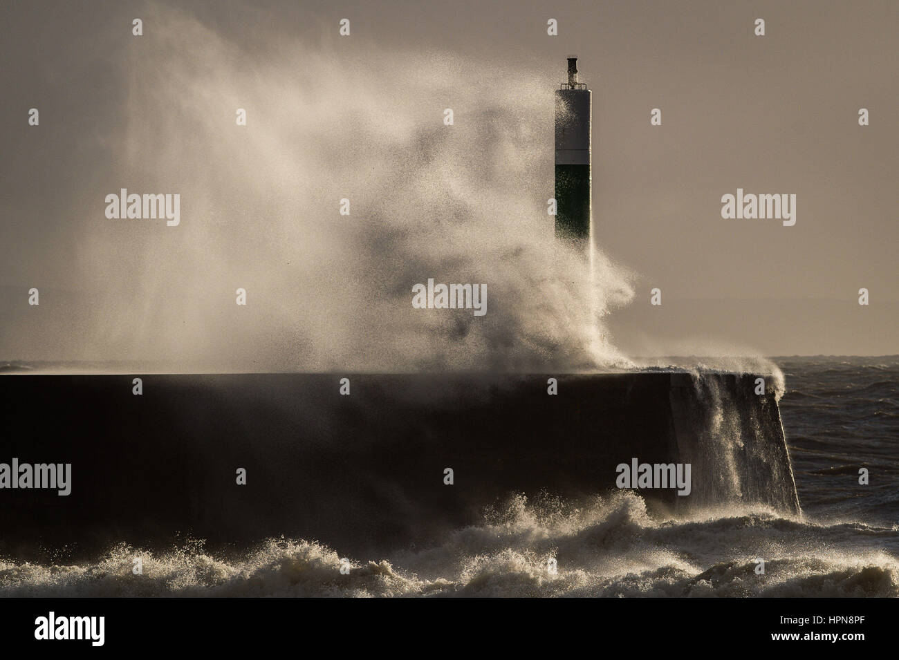 The lighthouse and harbour wall is battered by waves at Aberystwyth ...