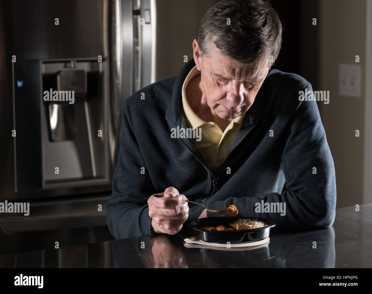 Lonely and depressed senior male sitting alone at kitchen table eating ...