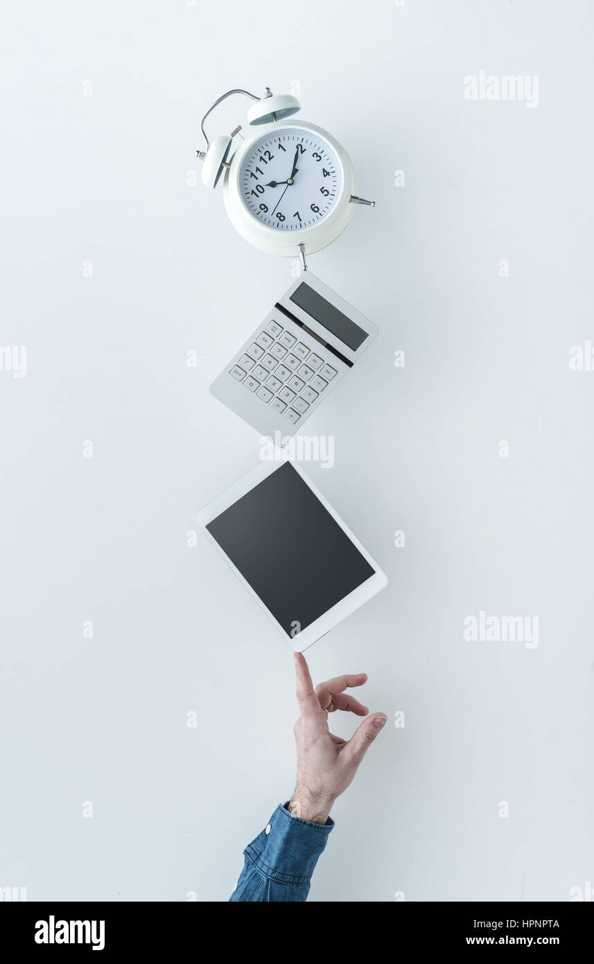 Casual businessman balancing a clock, a calculator and a digital tablet ...