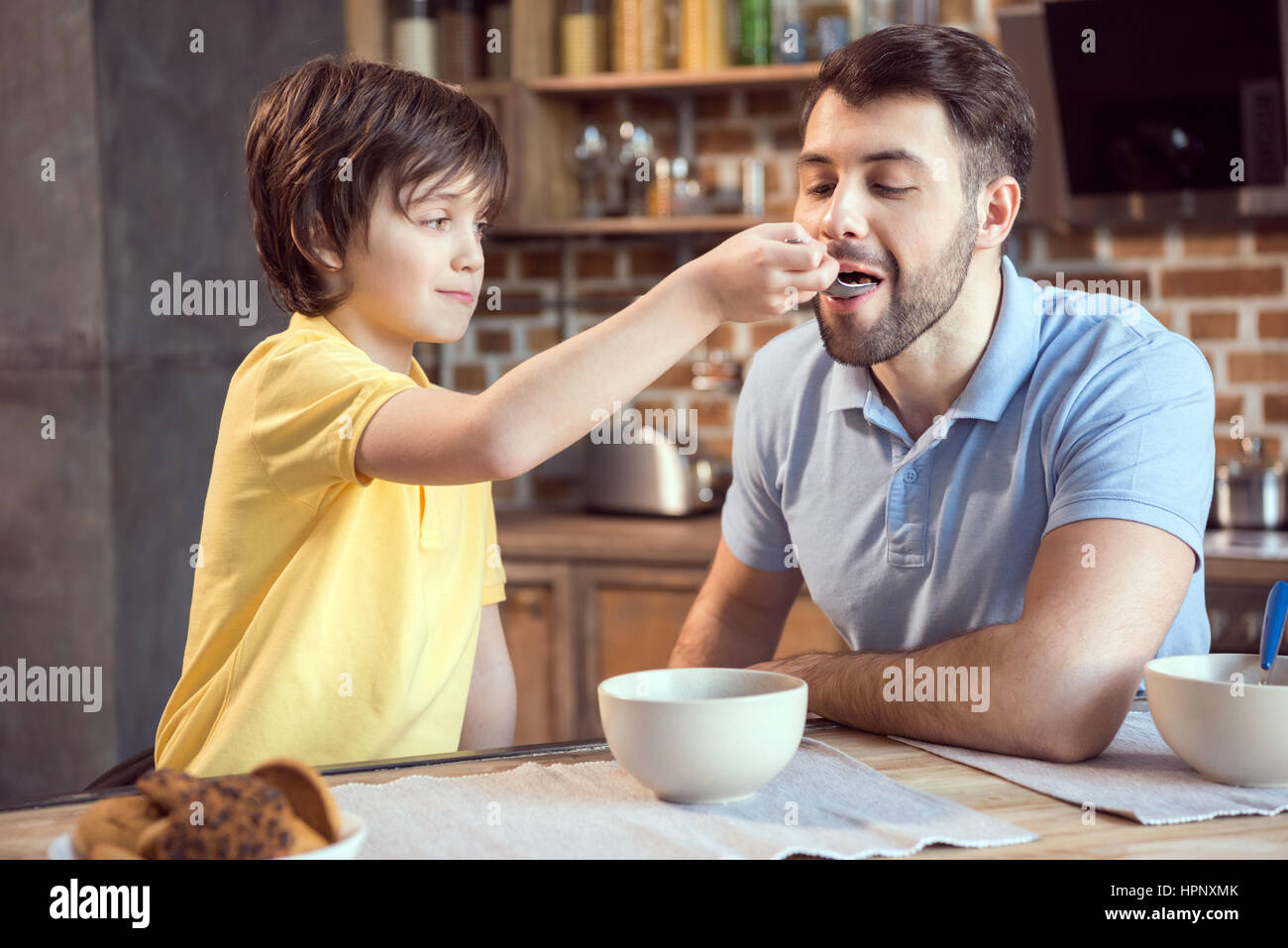 smiling boy feeding father with breakfast Stock Photo - Alamy