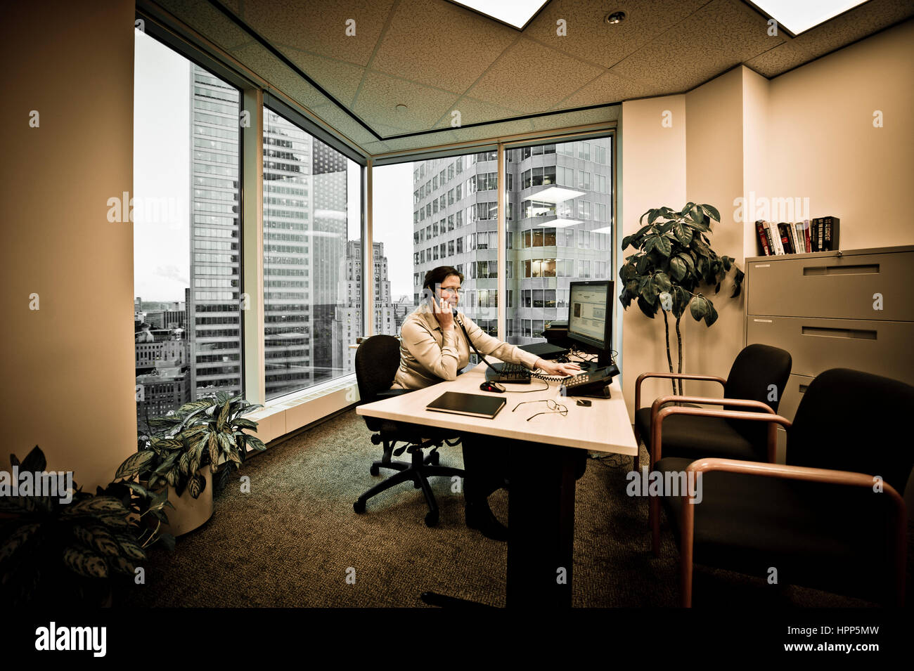 Business woman executive in a corner office sitting at the desk talking ...