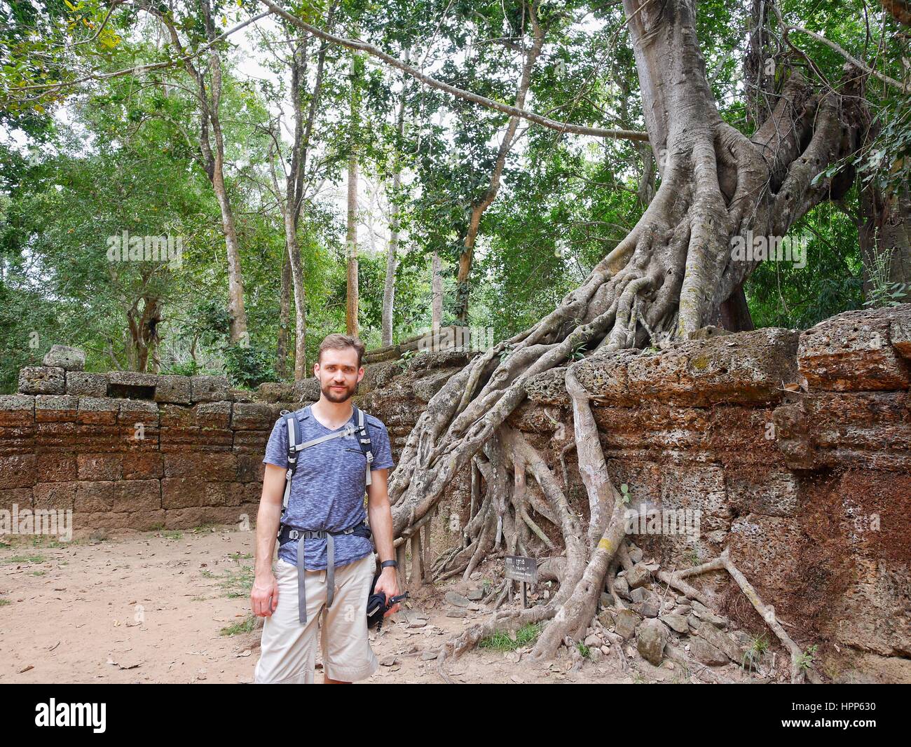 Man standing in front of a giant tree root at temple ruin site angkor ...