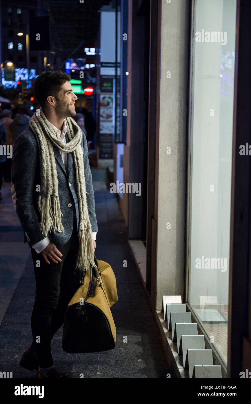 Smiling man with a bag looking in shop window at night Stock Photo - Alamy