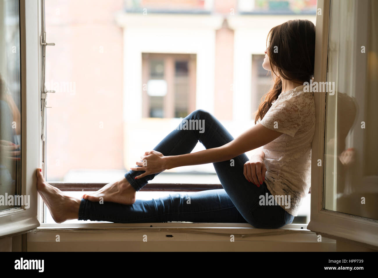 Woman sitting on window sill looking through open window Stock Photo ...