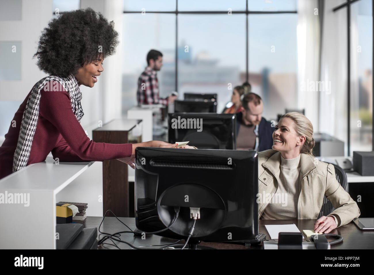 Casual female office worker handing over notes to coworker behind desk ...