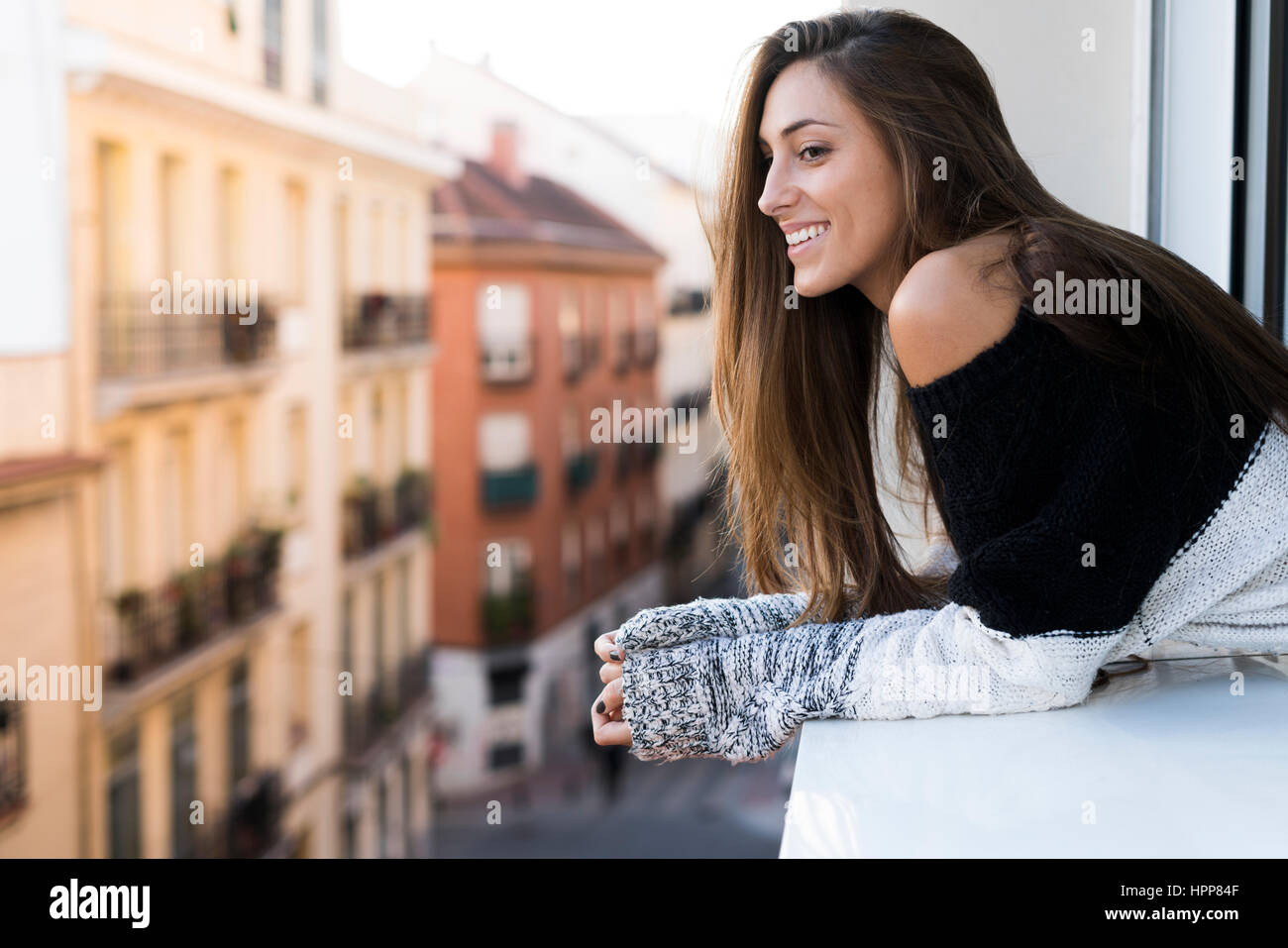 Smiling young woman leaning on window sill Stock Photo - Alamy