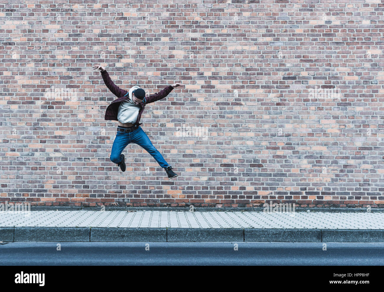 Young man jumping in front of brick wall Stock Photo - Alamy
