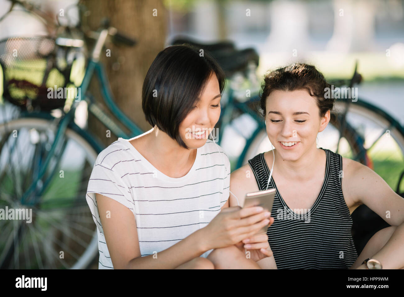 Two friends sitting in city park listening music together with ...