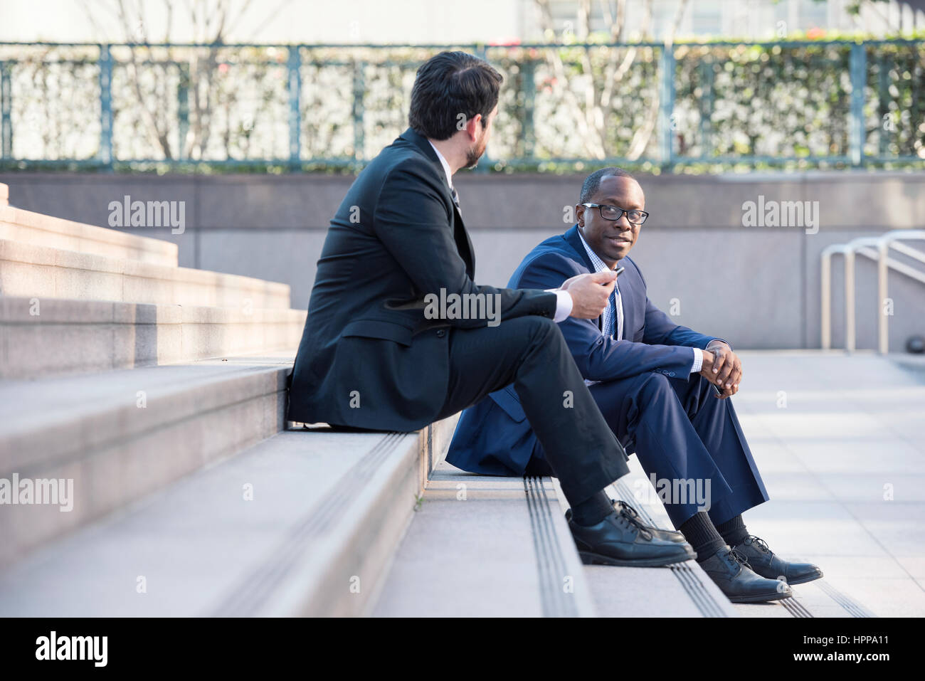 Two businessmen sitting on stairs talking Stock Photo - Alamy