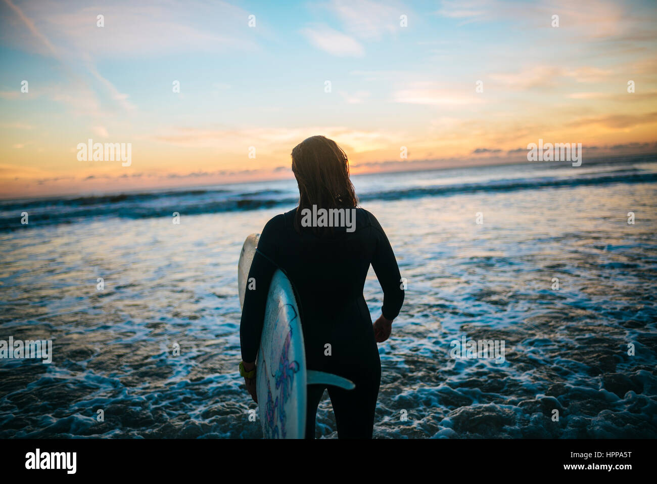 Back view of young woman with surfboard standing at seashore watching ...