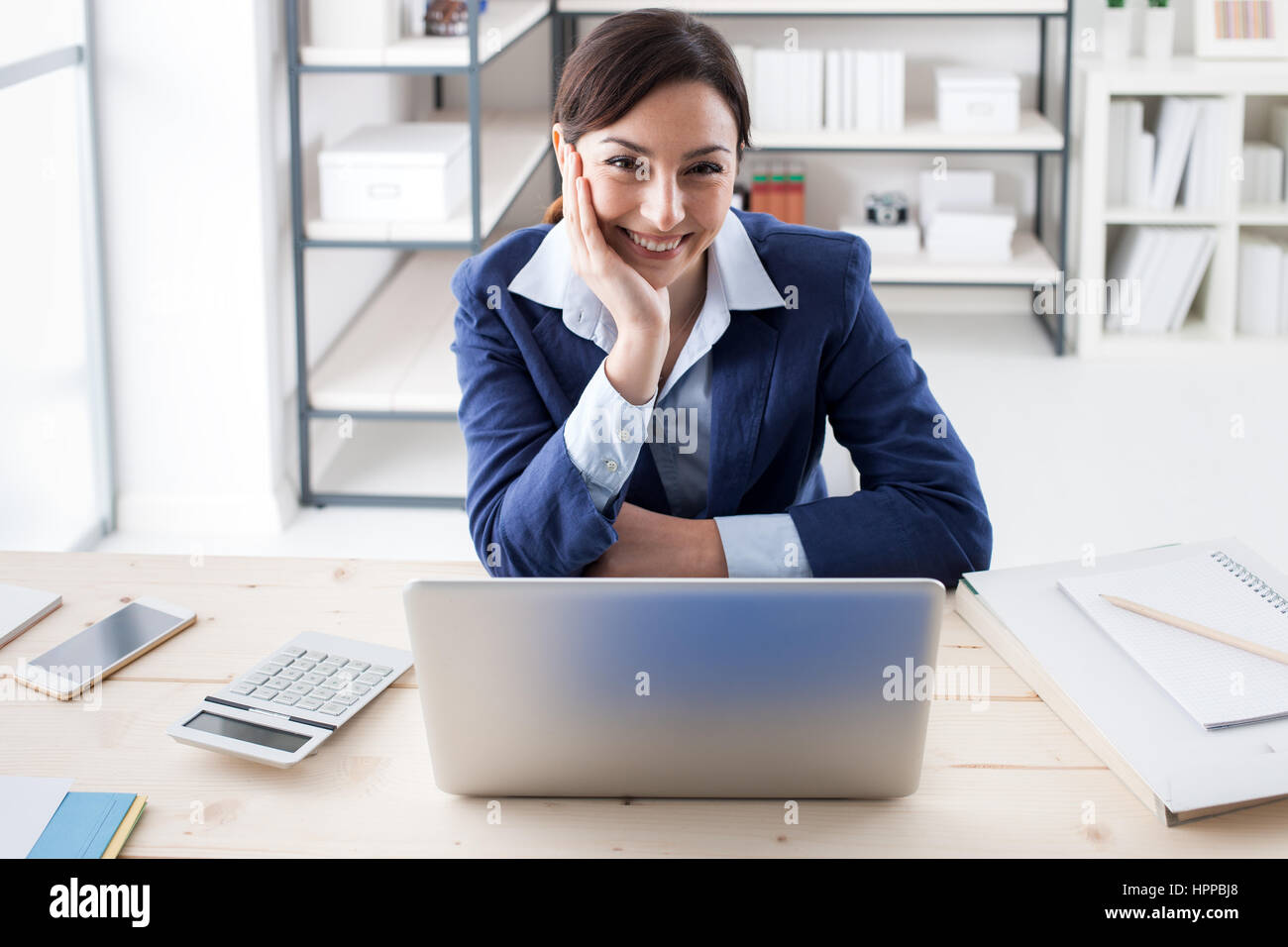 Confident smiling female executive posing in her office with hand on ...