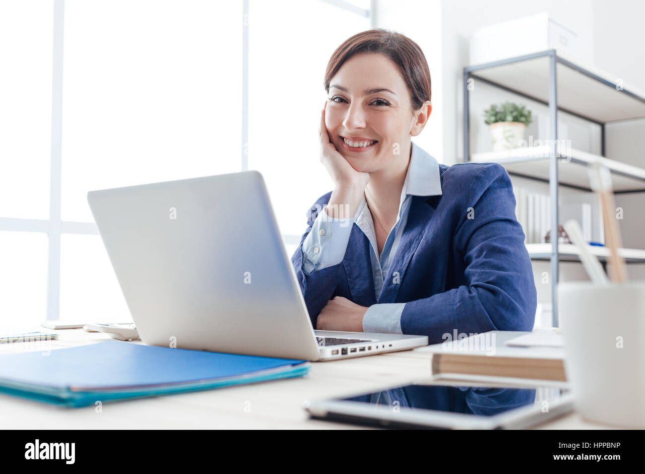 Confident smiling female executive posing in her office with hand on ...