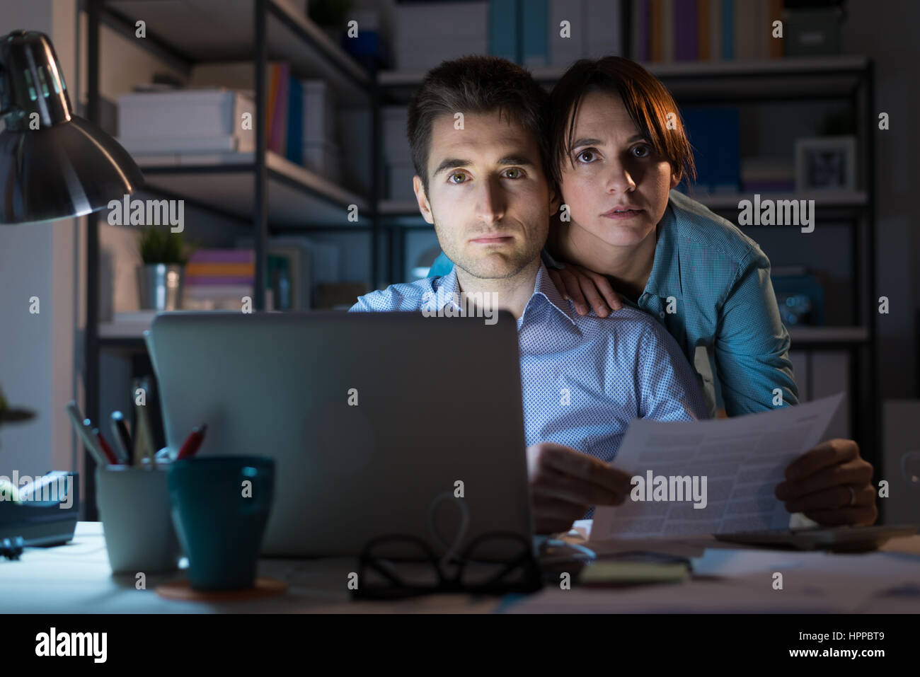 Young couple using a computer, checking bills and paperwork late at ...