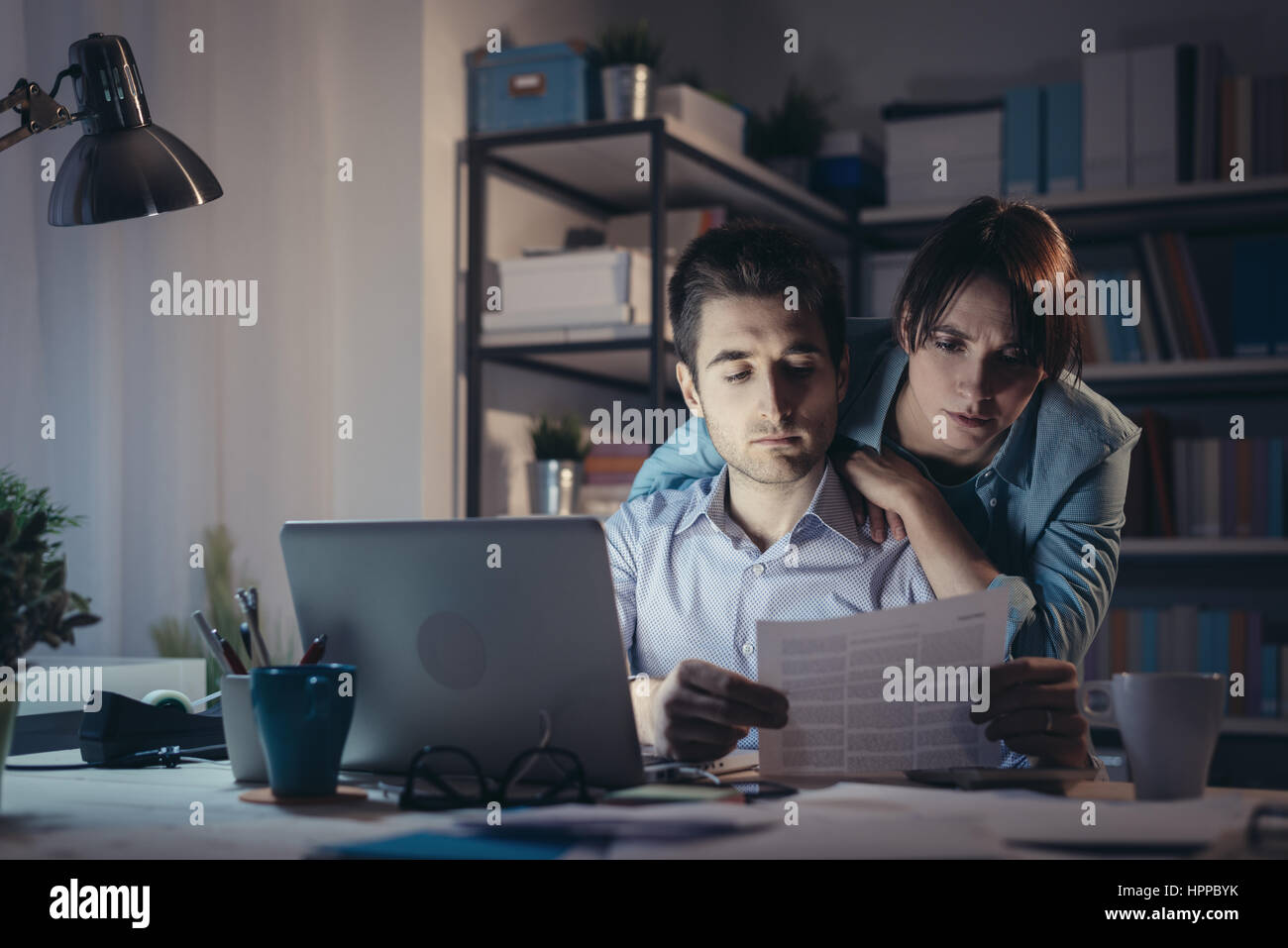 Young couple using a computer, checking bills and paperwork late at ...