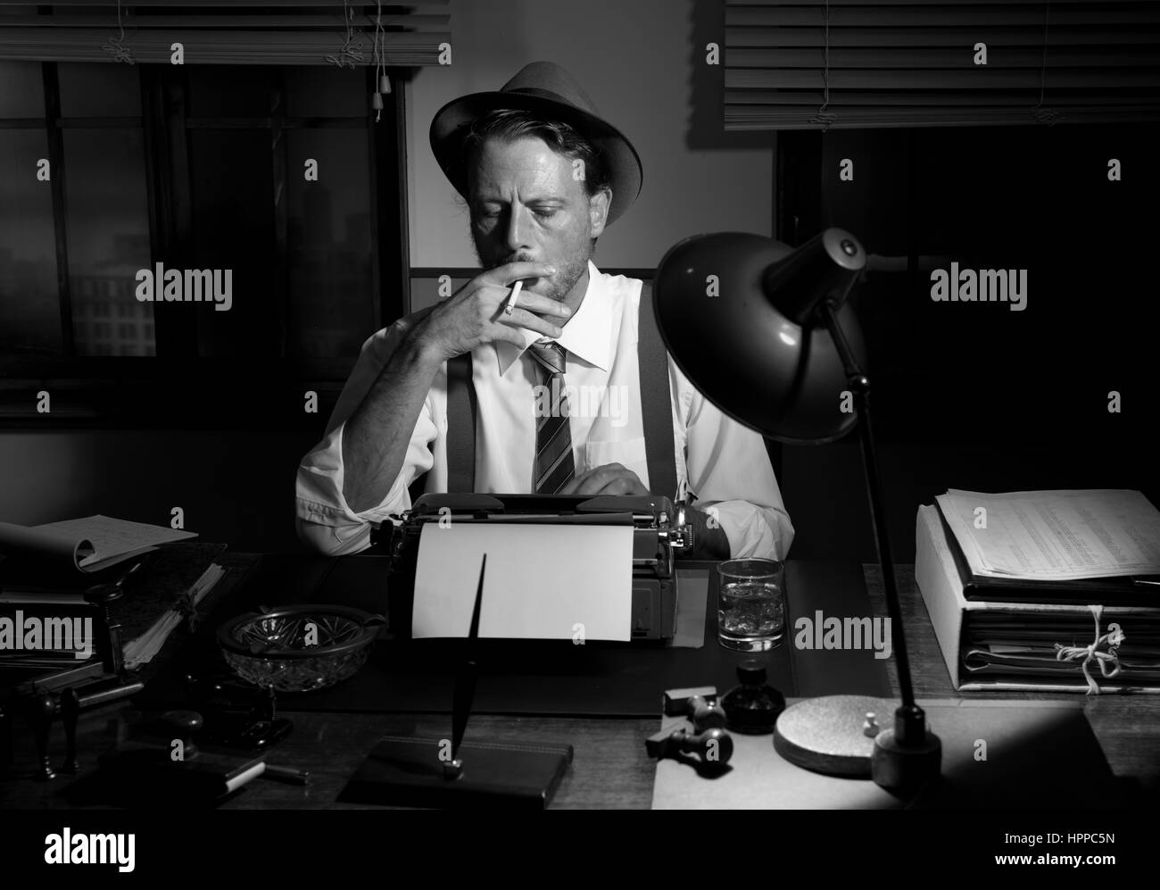 Retro reporter working late typing on a typewriter and smoking a ...