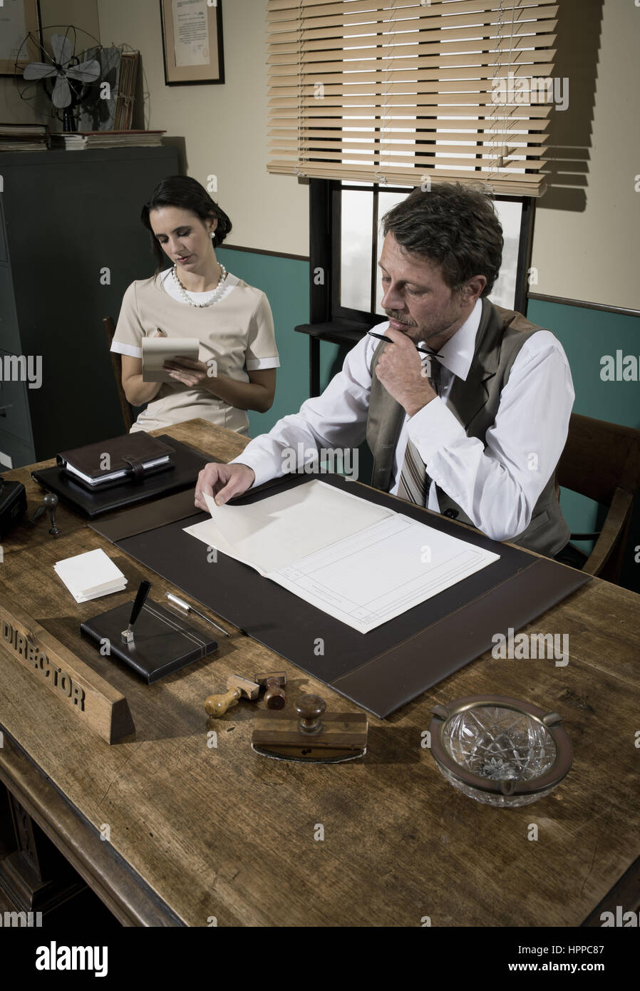 Director and secretary working together at desk, 1950s style office ...