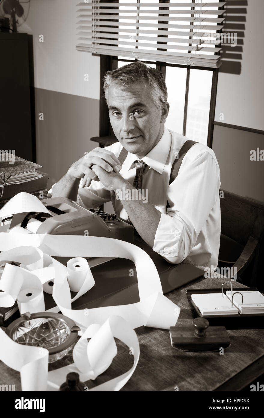Smiling professional accountant working at desk, 1950s style office ...
