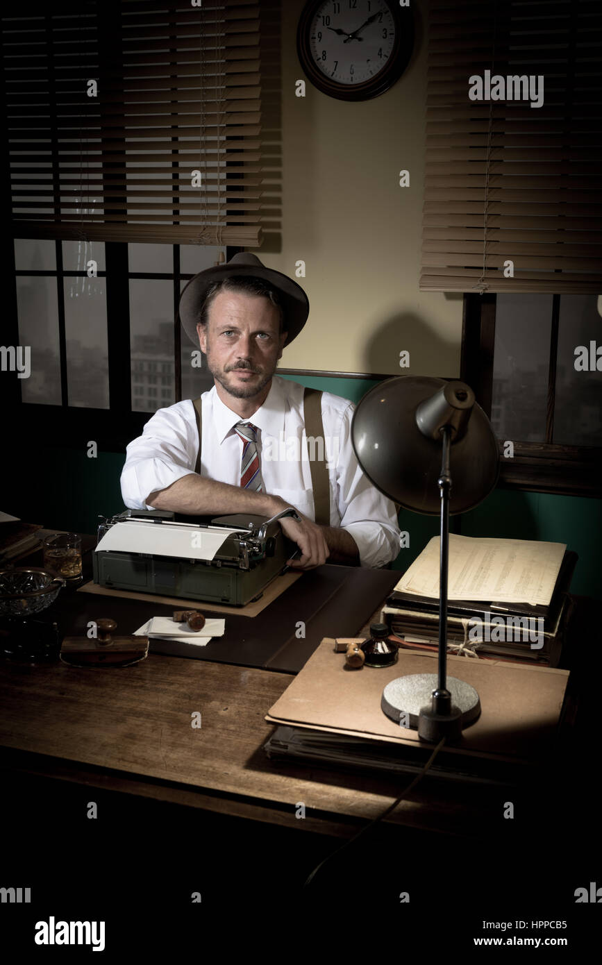 Retro reporter sitting at desk with typewriter posing and looking at ...