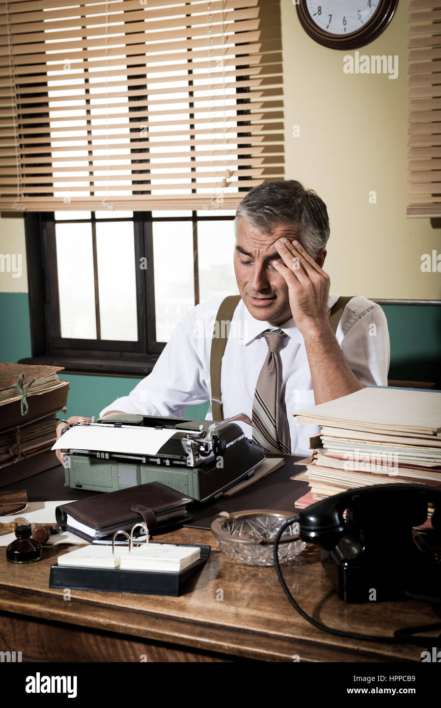 Exhausted reporter with headache working at office desk and touching ...